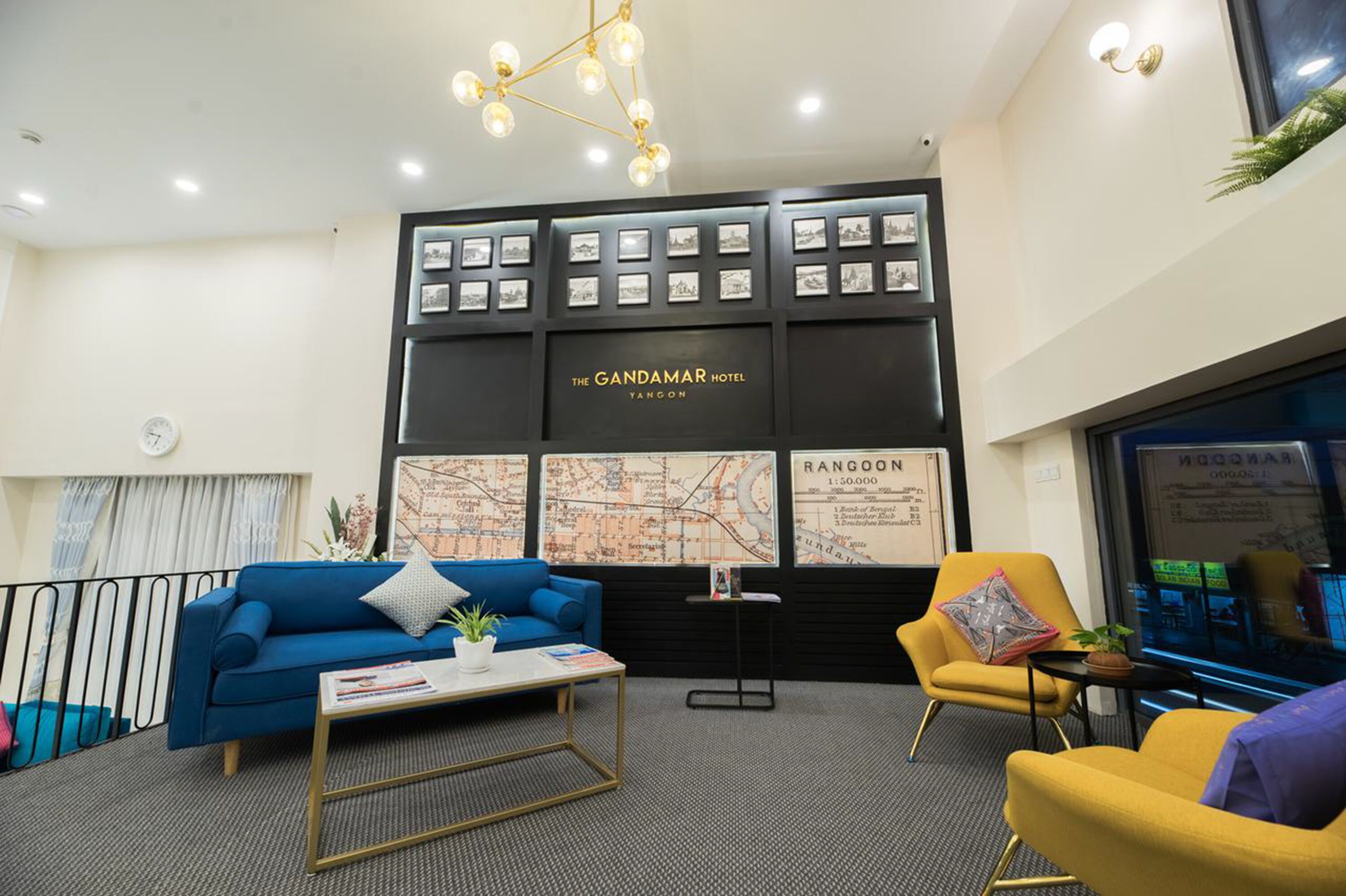 Um hall de entrada com um sofá azul, uma poltrona amarela, uma mesa de centro e uma parede com quadros e um mapa.