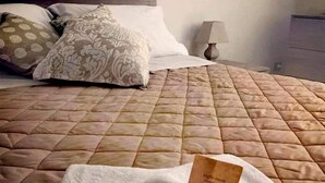 Cama bem arrumada com manta acolchoada, um cobertor branco e duas barras de chocolate Dolce Vita.