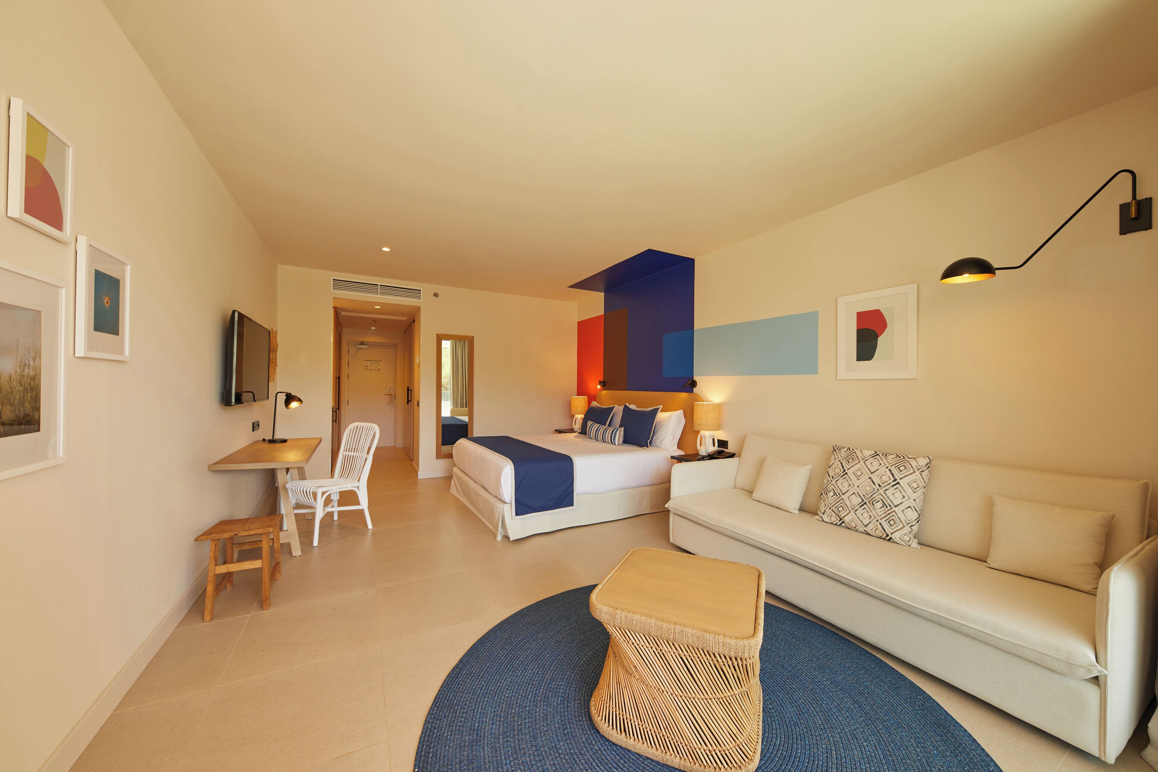 Quarto de hotel moderno com uma cama, um sofá branco, uma mesinha e uma escrivaninha.