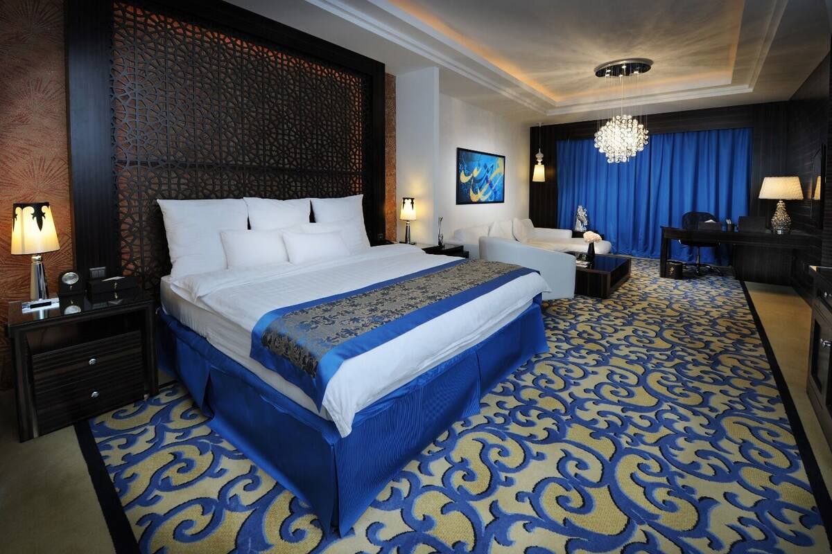 Quarto de hotel com cama grande, sofá, escrivaninha e um candelabro.
