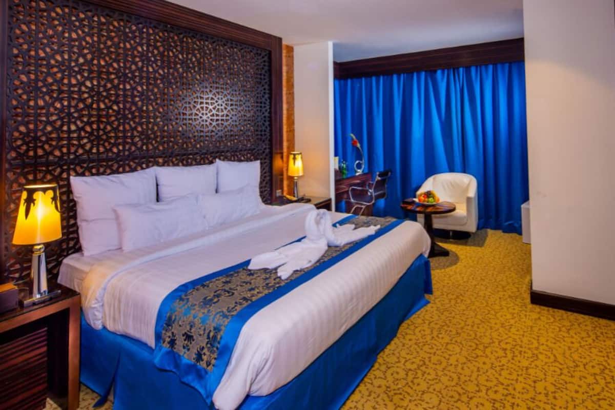 Quarto de hotel com uma cama grande, uma escrivaninha com cadeira, uma televisão e uma cortina azul.