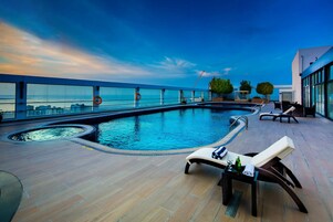 Piscina no terraço com espreguiçadeiras e vista para a cidade.