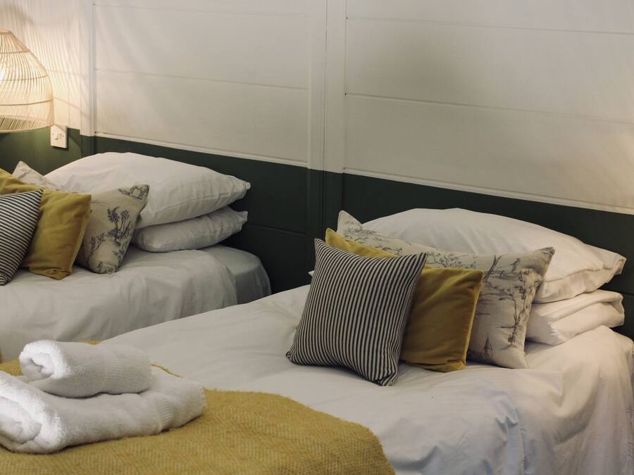 Quarto de hotel com duas camas, cada uma com lençóis brancos e várias almofadas. Há duas luminárias pendentes sobre as camas.