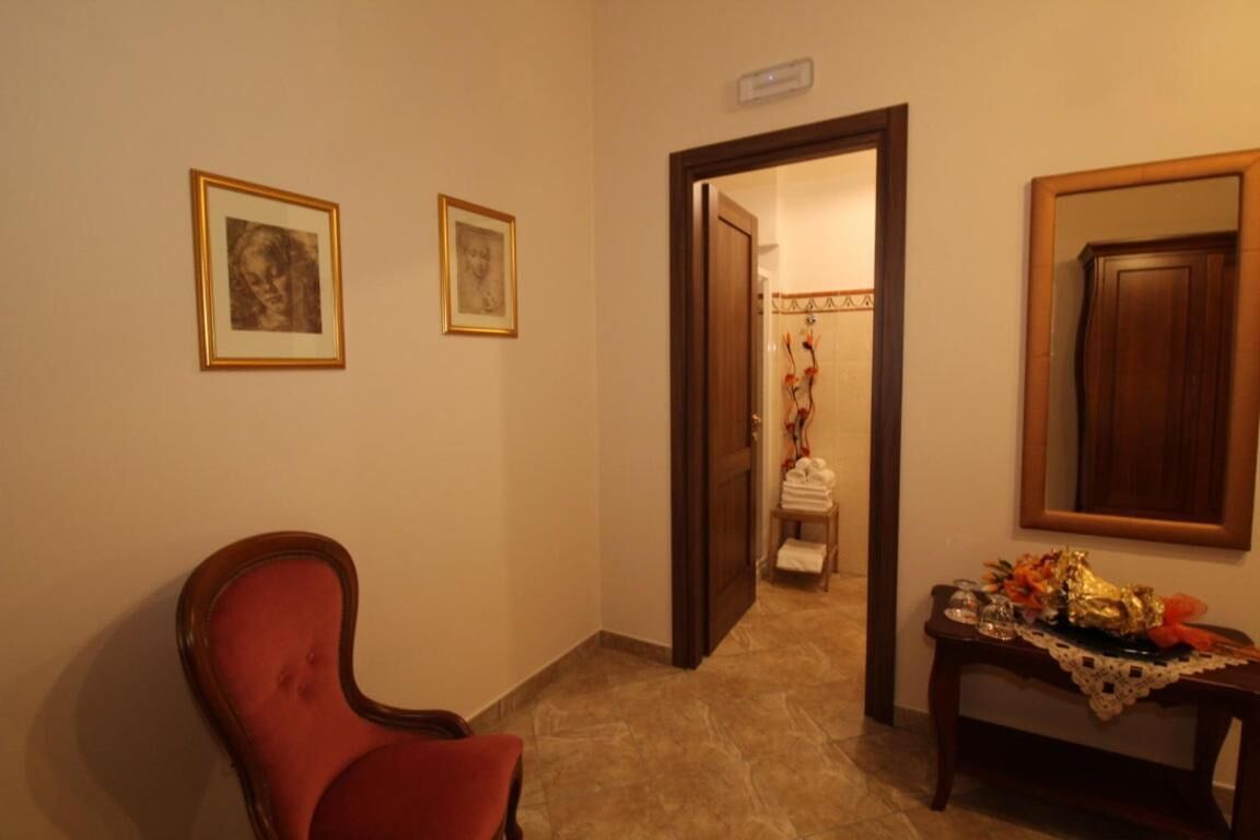 Um corredor com uma cadeira vermelha, um banco de madeira com um objeto decorativo e duas fotos emolduradas na parede.