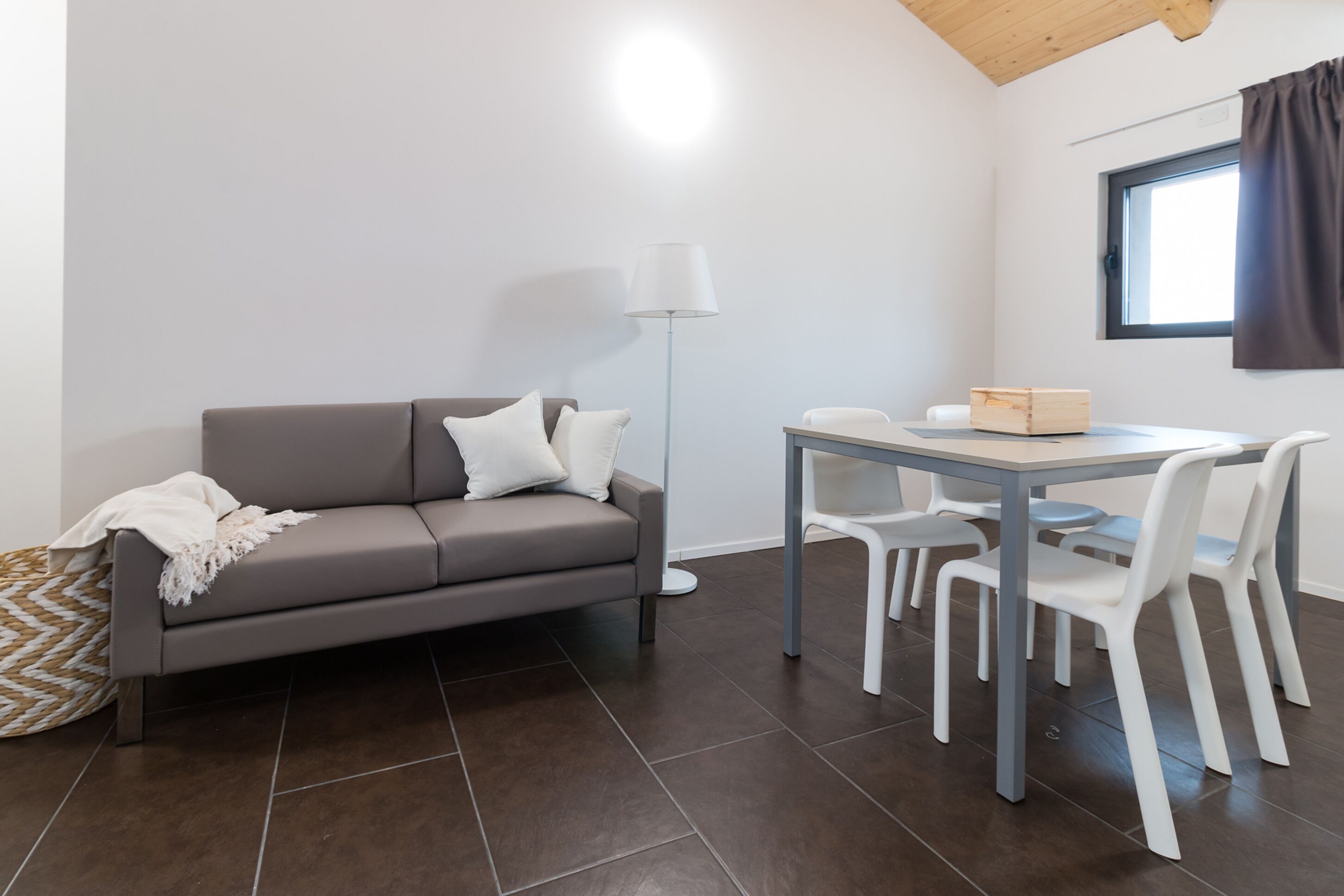 Uma sala de estar moderna com um sofá cinzento, cadeiras brancas, uma pequena mesa e um abajur.
