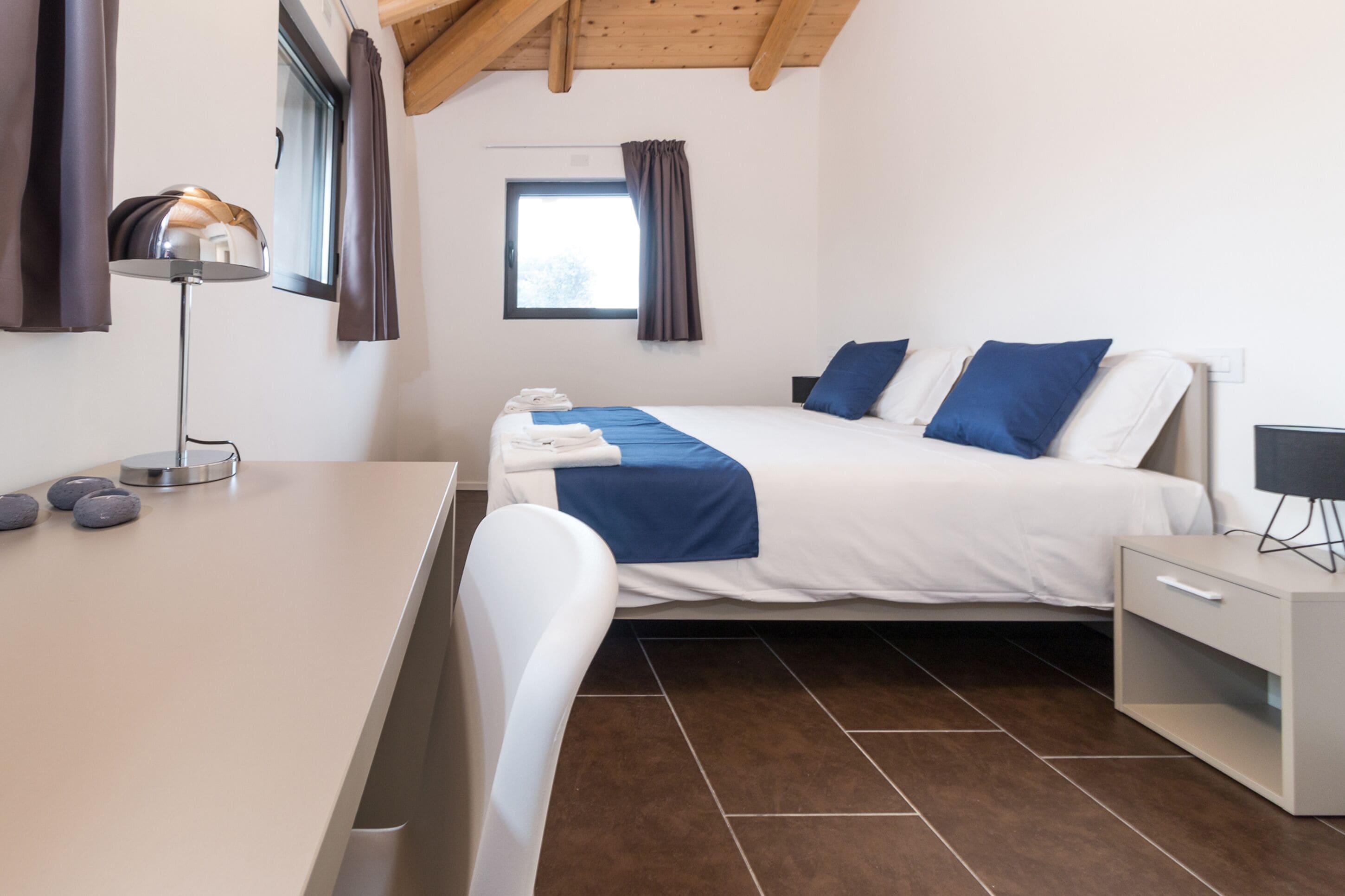 Quarto de hotel moderno com uma cama, mesa de cabeceira e uma escrivaninha com abajur.