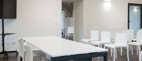 Uma sala de conferências com mesa e cadeiras brancas, uma TV de tela plana e uma porta com painel de vidro.