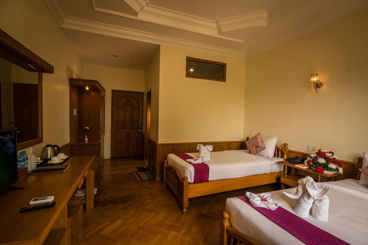 Quarto de hotel com duas camas, uma escrivaninha de madeira, uma televisão e um banheiro visível através de uma porta aberta.