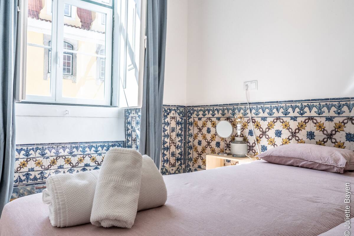 Quarto de hotel com cama, mesa de cabeceira, espelho e janela com cortinas.