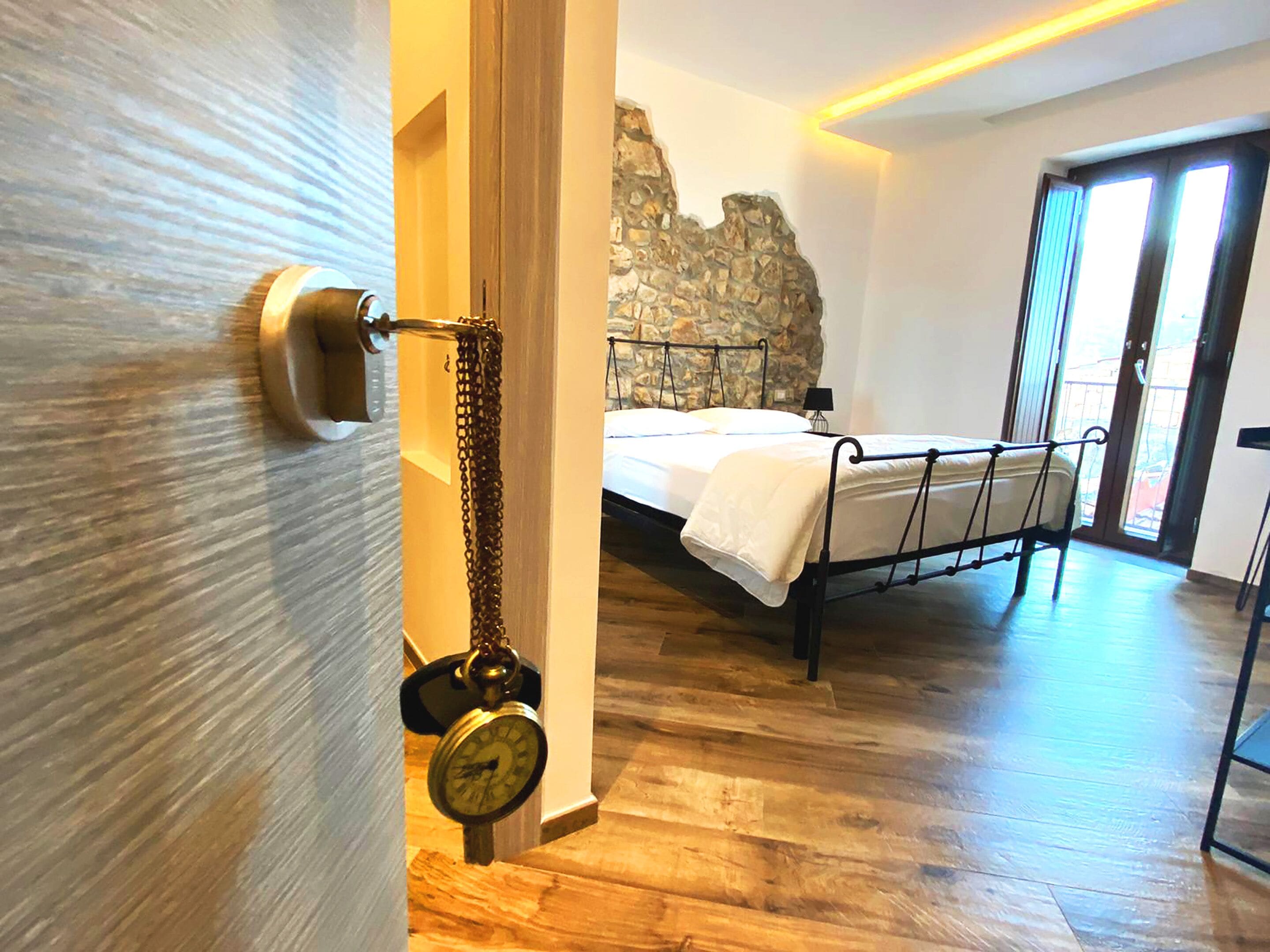 Quarto com parede de pedra, cama com estrutura de metal e chão de madeira.