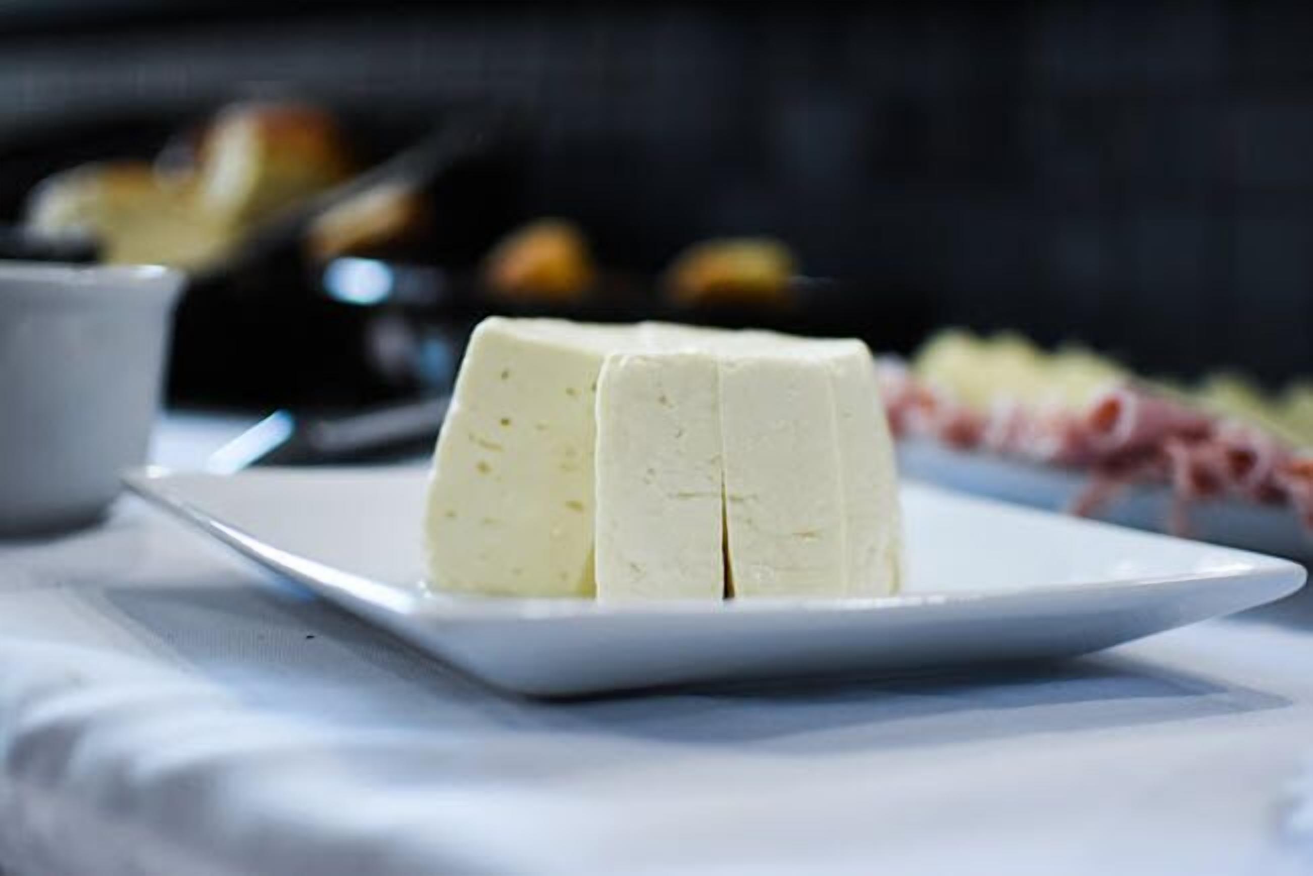 Um prato branco com uma fatia triangular de queijo sobre uma toalha de mesa.