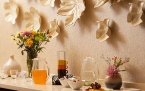 Mesa posta para o café da manhã, com um vaso de flores, cafeteira e diversos copos e tigelas.