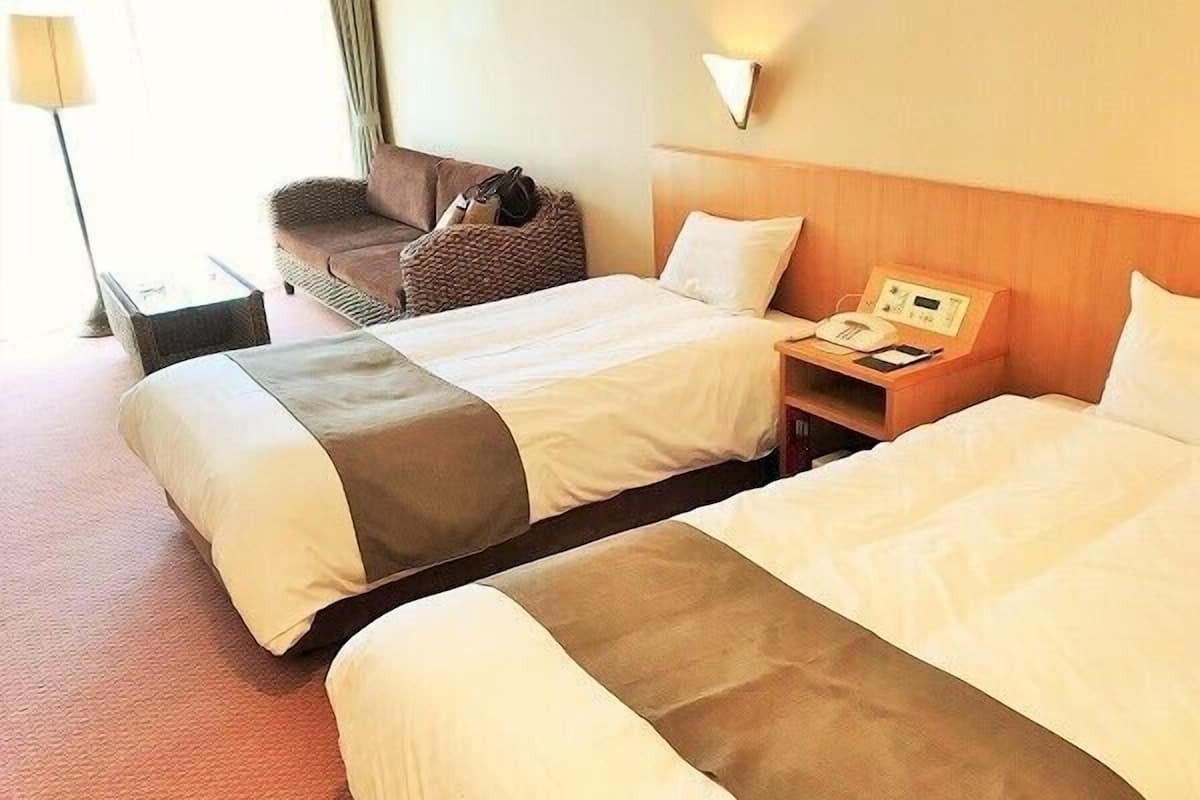 Quarto de hotel com duas camas, um sofá, uma luminária e uma mesa de cabeceira com telefone.