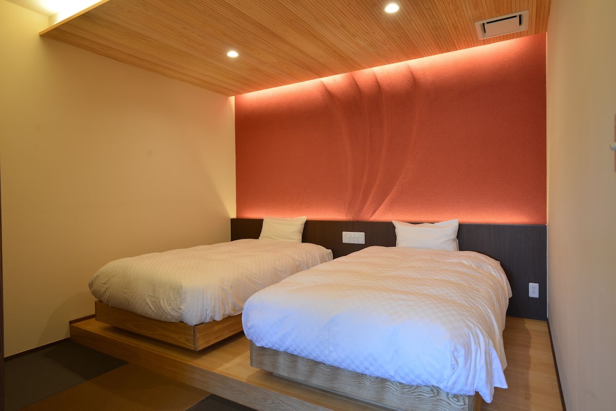 Quarto com duas camas, piso de madeira e parede em destaque vermelha.