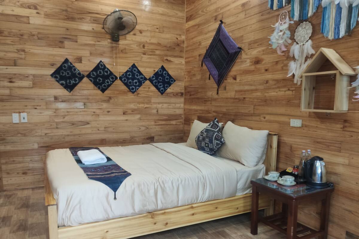 Quarto com painéis de madeira, uma cama, uma mesinha com chaleira e decorações nas paredes.