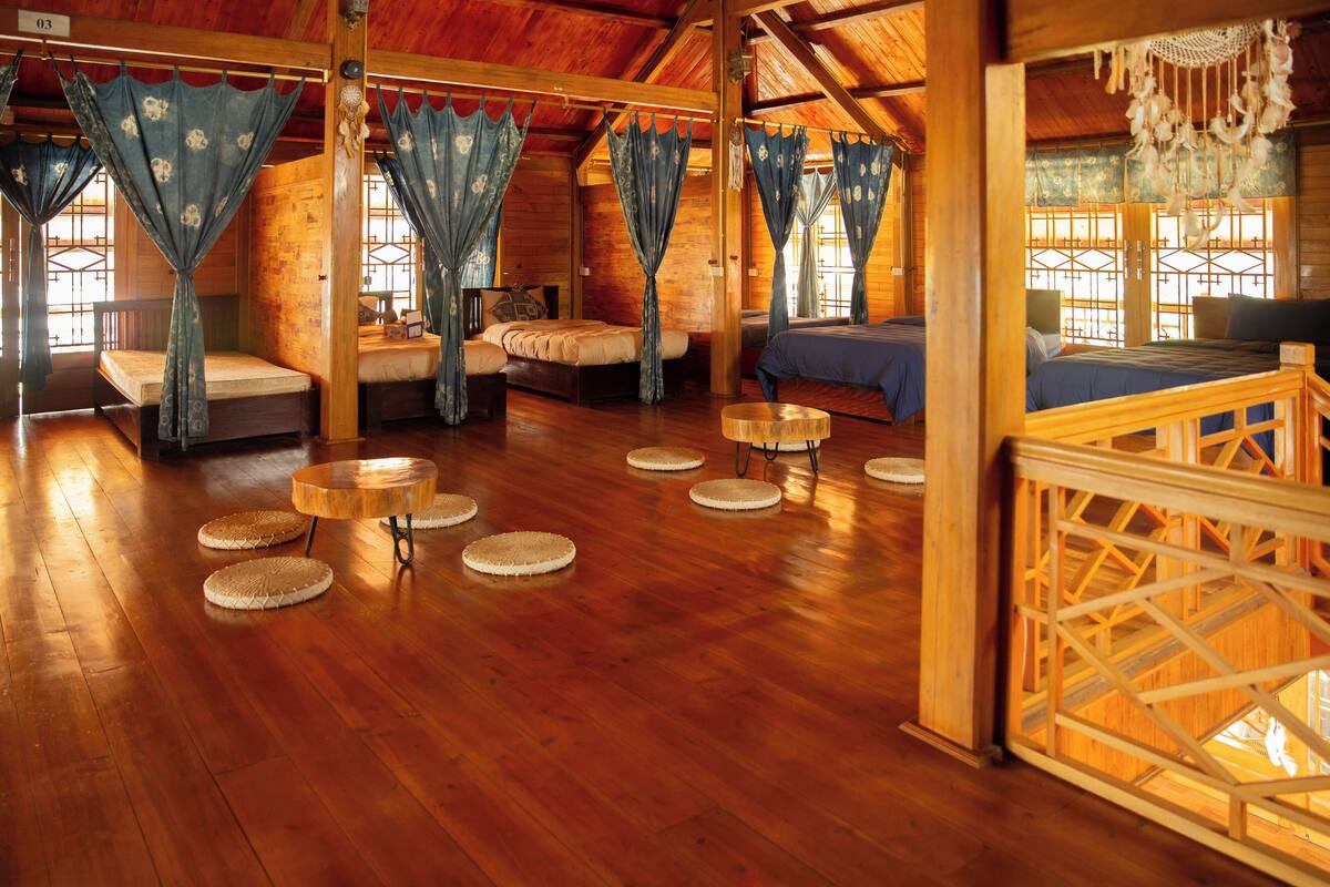 Um quarto espaçoso com piso de madeira, quatro camas com cortinas azuis e um corrimão de madeira.
