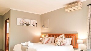 Quarto bem arrumado com cama, mesa de cabeceira e ar condicionado.