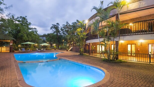 Uma piscina com um caminho de tijolos, cercada por palmeiras e um edifício com varandas.