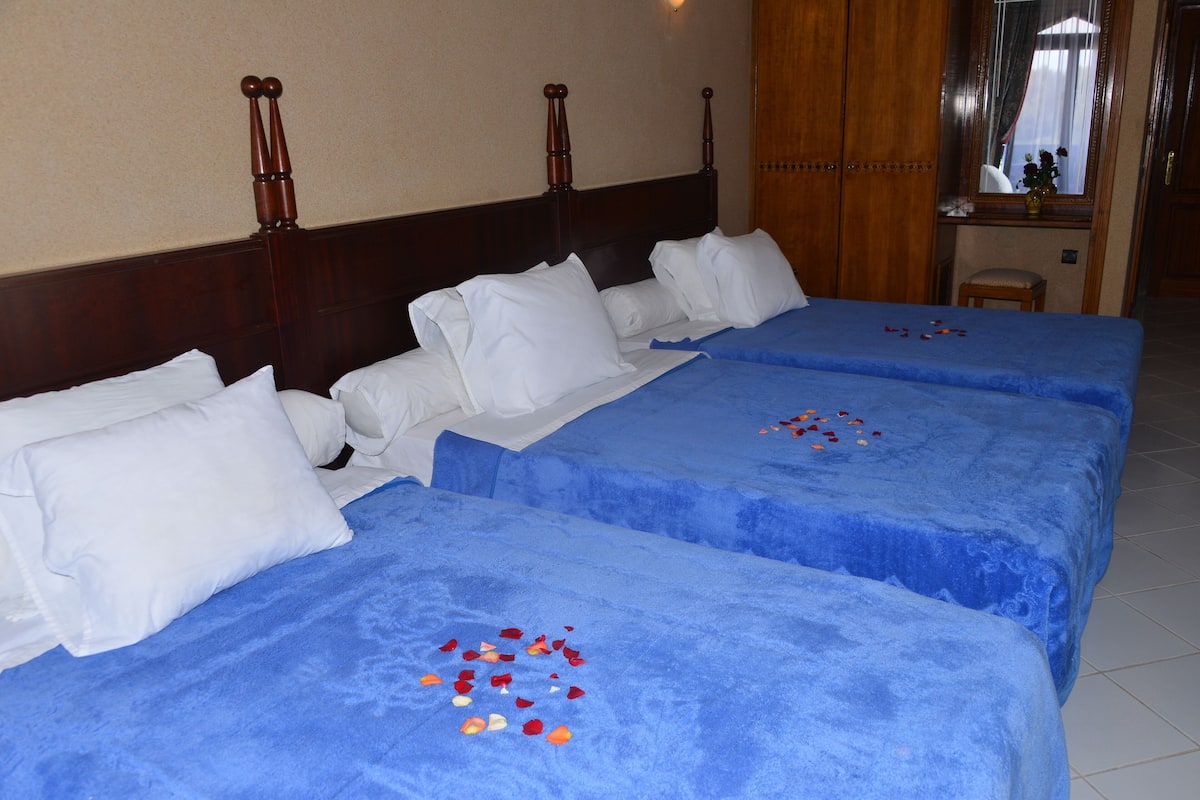 Quarto de hotel com duas camas, cada uma com colchas azuis e almofadas brancas.