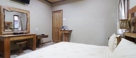 Quarto com cama grande, escrivaninha de madeira e TV fixada na parede.
