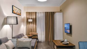 Um quarto moderno e bem iluminado, com um sofá, uma mesa pequena, uma cadeira, uma luminária e uma TV.