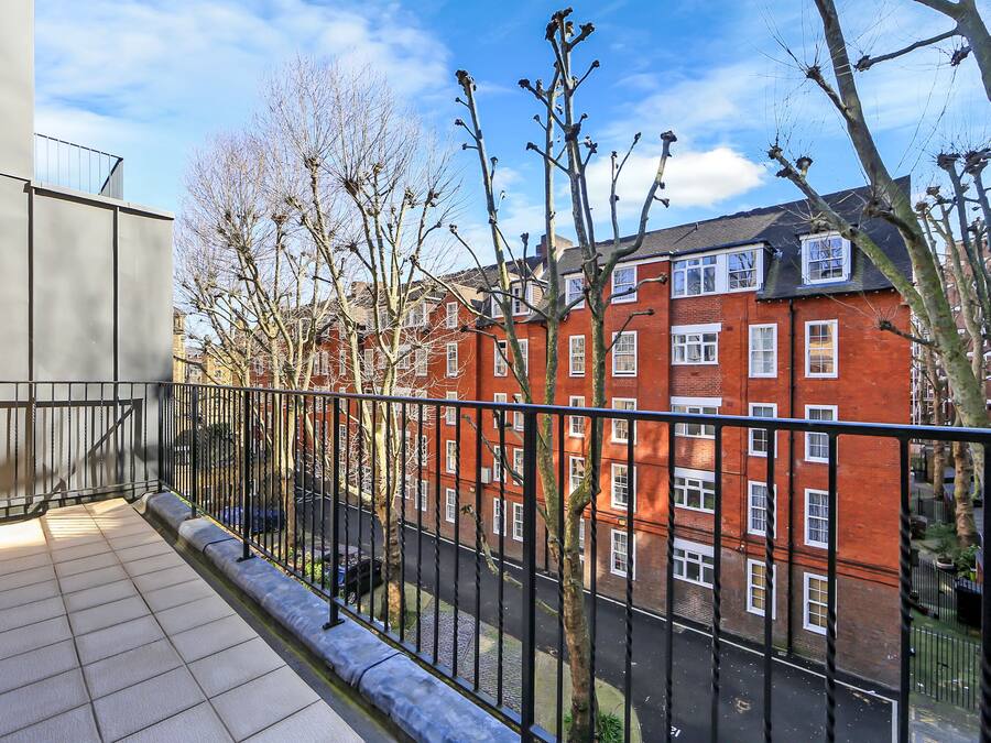 Varanda com guarda-corrimão de metal, vista para uma rua com edifícios de tijolos vermelhos e árvores sem folhas.