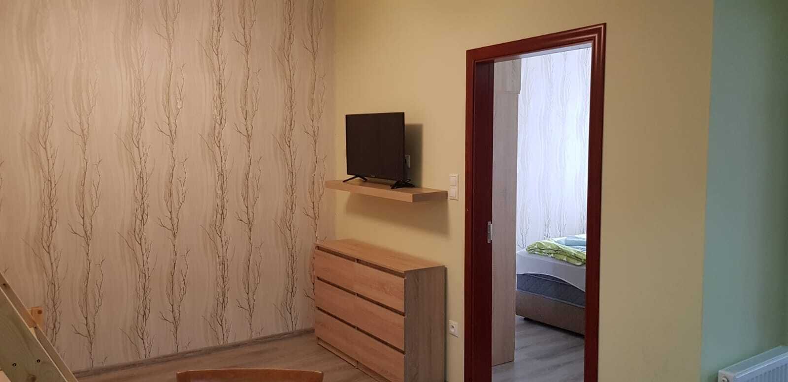 Um quarto com uma TV em uma prateleira, cômoda de madeira e uma cama com cobertor verde.