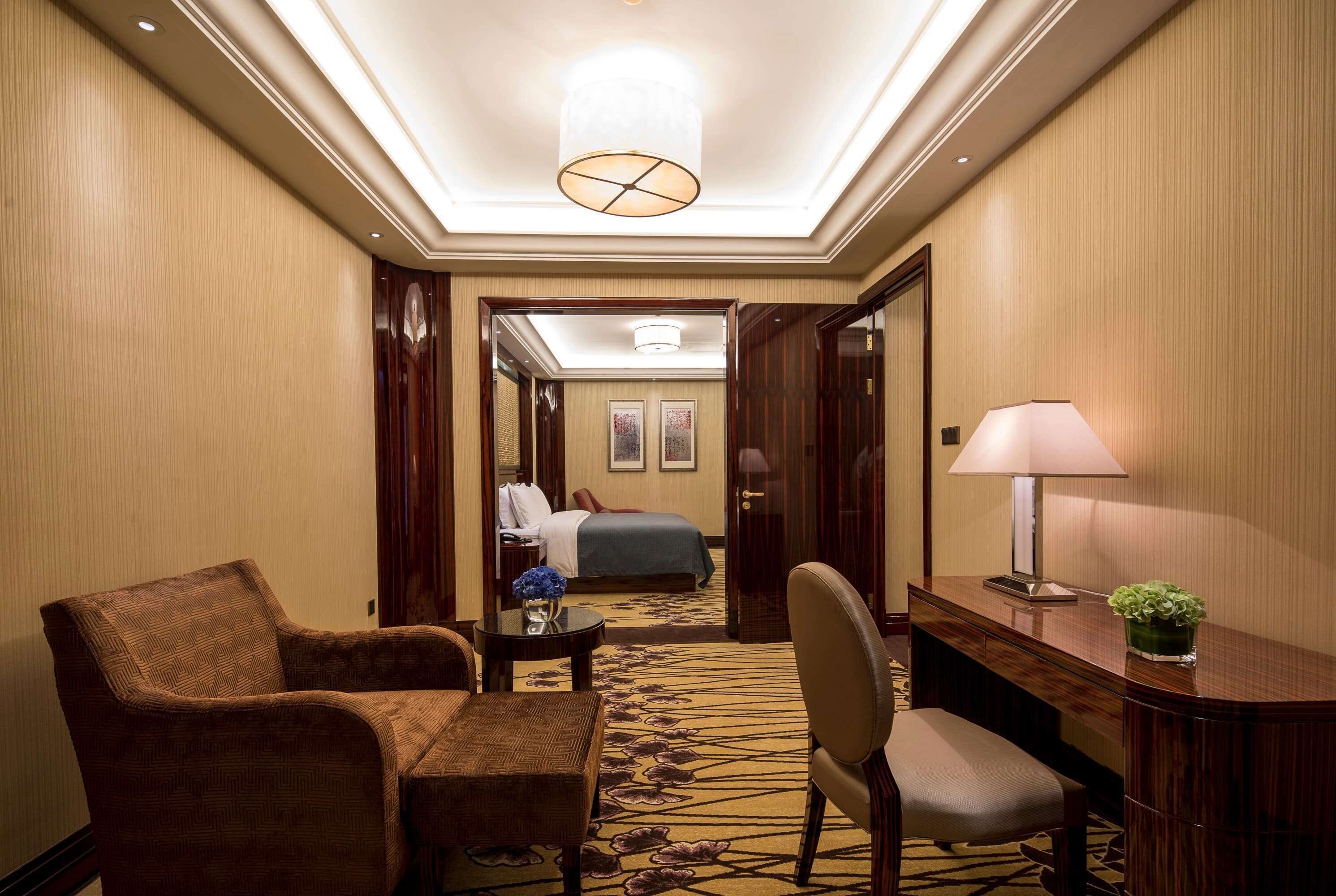 Quarto de hotel com cama, escrivaninha, cadeira, mesinha com um vaso e abajur.
