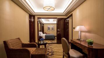 Quarto de hotel com cama, escrivaninha, cadeira, mesinha com um vaso e abajur.