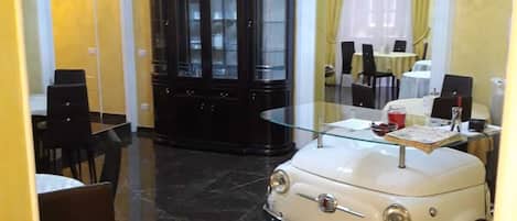 Uma área de refeições com mesa de vidro, cadeiras pretas, um armário preto e um objeto em forma de carro branco.