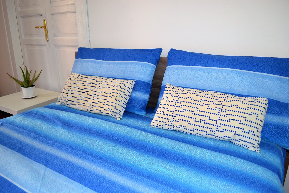 Cama com roupa de cama azul e duas almofadas estampadas com poás.