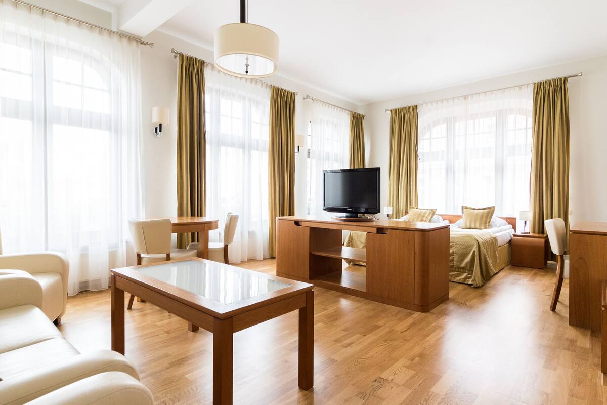 Quarto de hotel com escrivaninha de madeira, televisão, sofá e cama com cortinas.