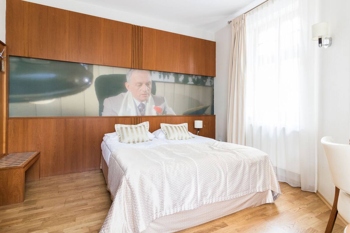 Quarto de hotel com uma cama grande, lambris de madeira, televisão e escrivaninha com cadeira.