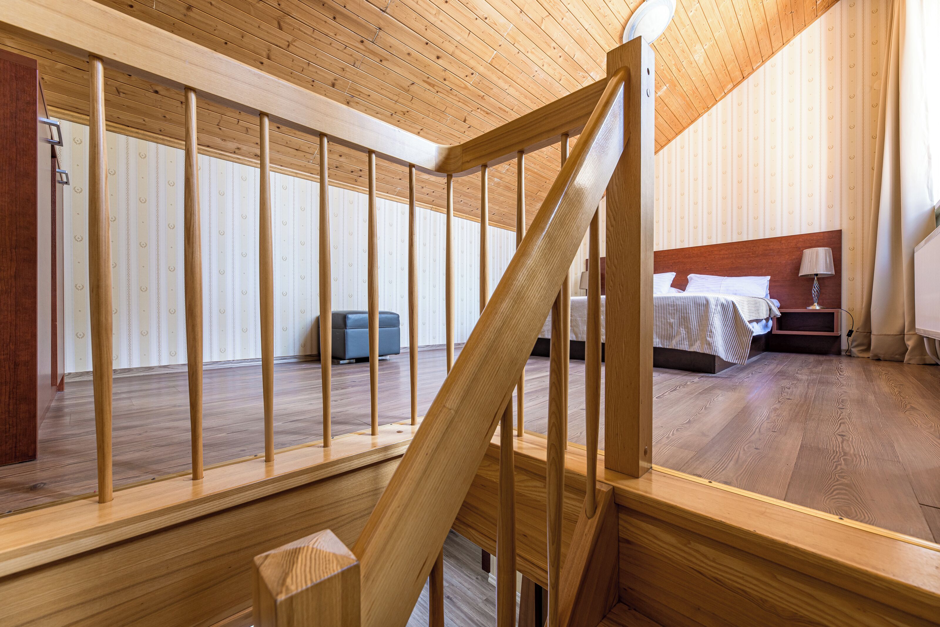 Um quarto espaçoso com escada de madeira, uma cama com cabeceira de madeira, uma mesa de cabeceira e um abajur.