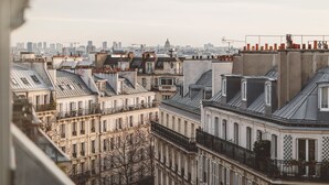 Vista de prédios parisienses com várias sacadas e um horizonte urbano ao fundo.