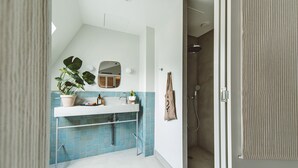 Casa de banho com lavatório branco, azulejos azuis, uma planta em vaso e chuveiro.