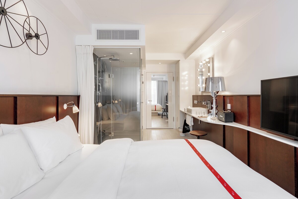 Quarto de hotel com uma cama grande, toucador com espelho, televisão e closet espaçoso.