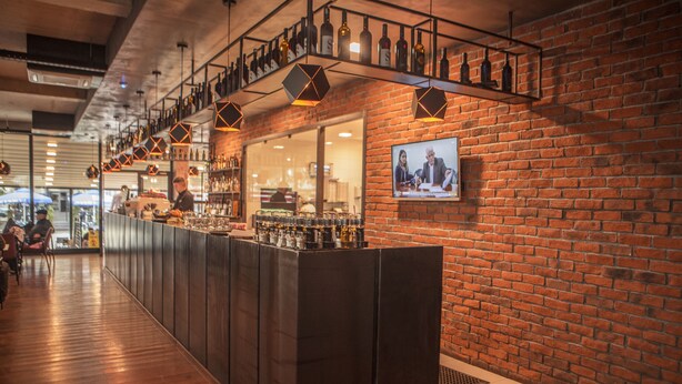 Uma área de bar com um balcão comprido, prateleiras com garrafas e uma parede de tijolos.