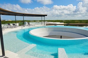 Uma piscina com design circular, rodeada por espreguiçadeiras e uma área de estar coberta.