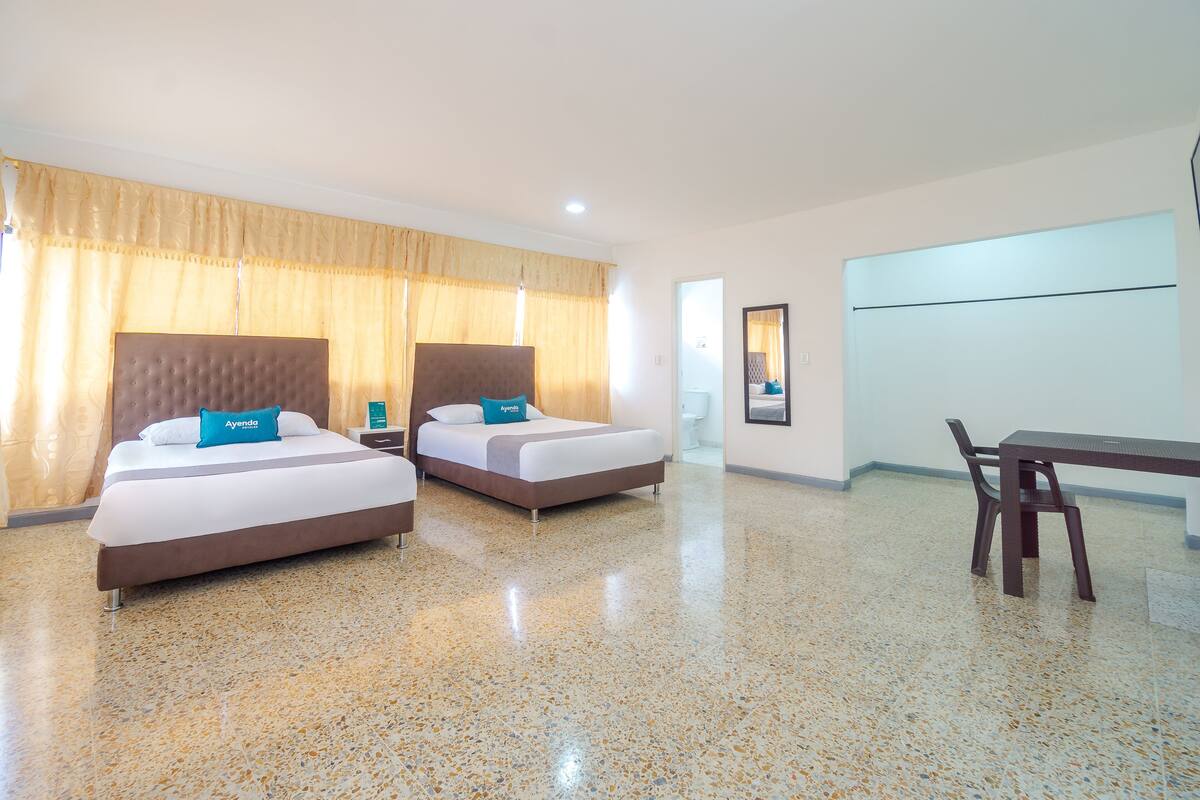 Quarto de hotel com duas camas, uma mesa e uma cadeira.