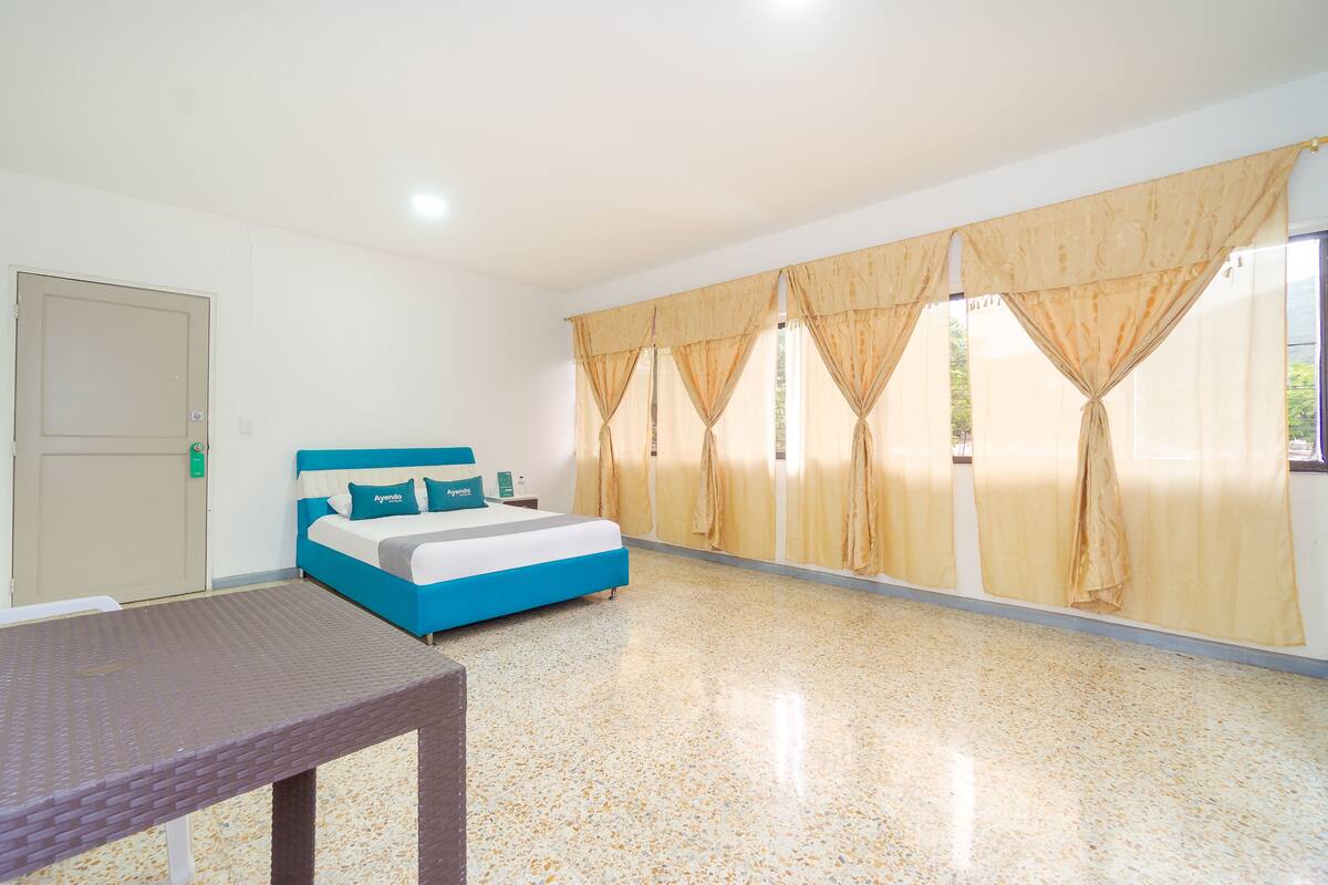 Quarto de hotel com cama, mesa e janelas amplas com cortinas.