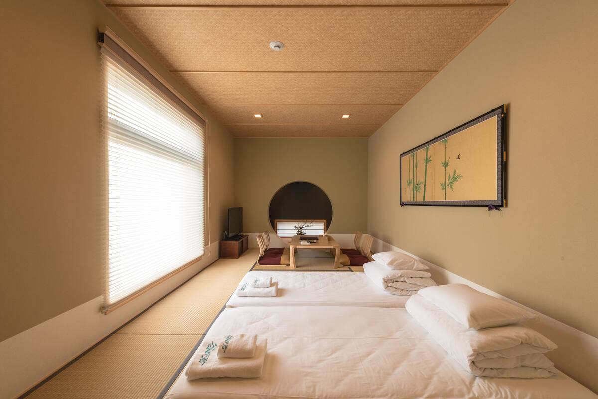 Quarto de hotel com duas camas, um futon, uma televisão e um quadro na parede.
