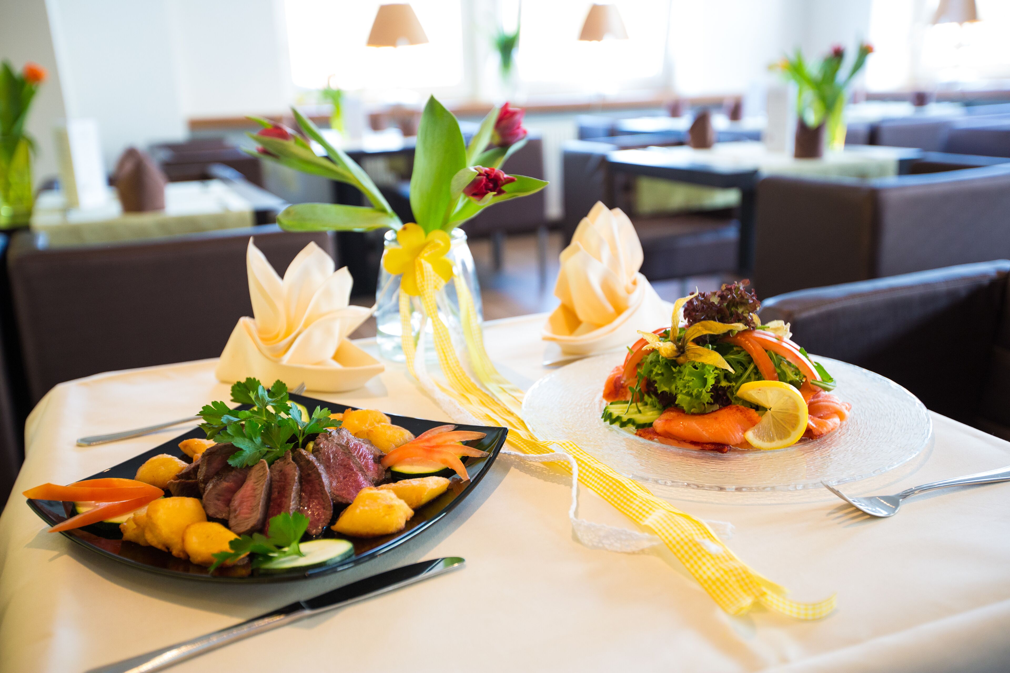 Uma mesa de jantar com dois pratos de comida, um vaso com flores e um guardanapo amarelo.