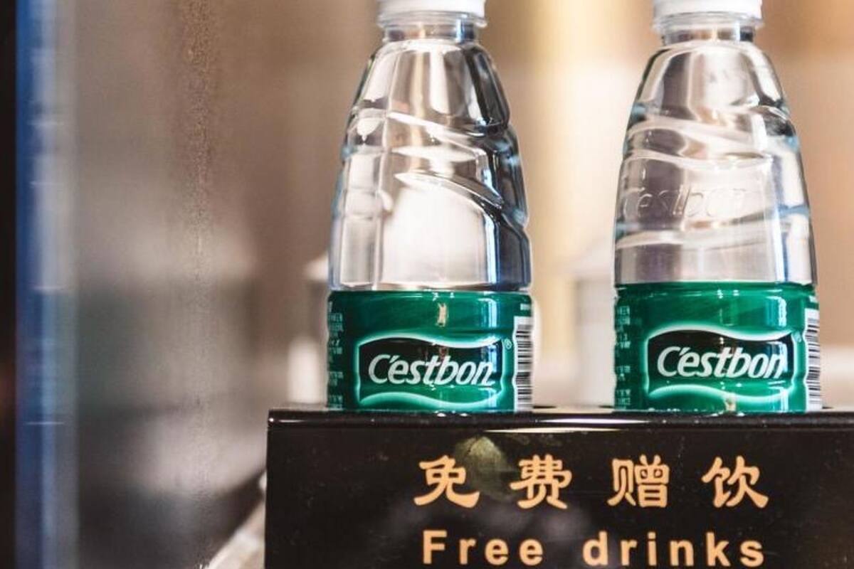 Duas garrafas de água C'estbon sobre um suporte preto com um letreiro que diz 'Bebidas Gratuitas'.