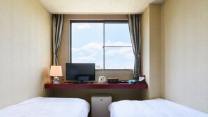 Quarto de hotel com duas camas, uma escrivaninha com computador, uma luminária e uma janela com cortinas.