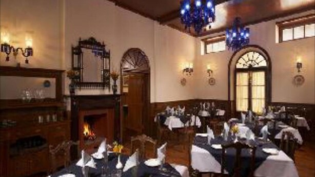Uma sala de jantar com mesas postas, uma lareira e um candelabro.
