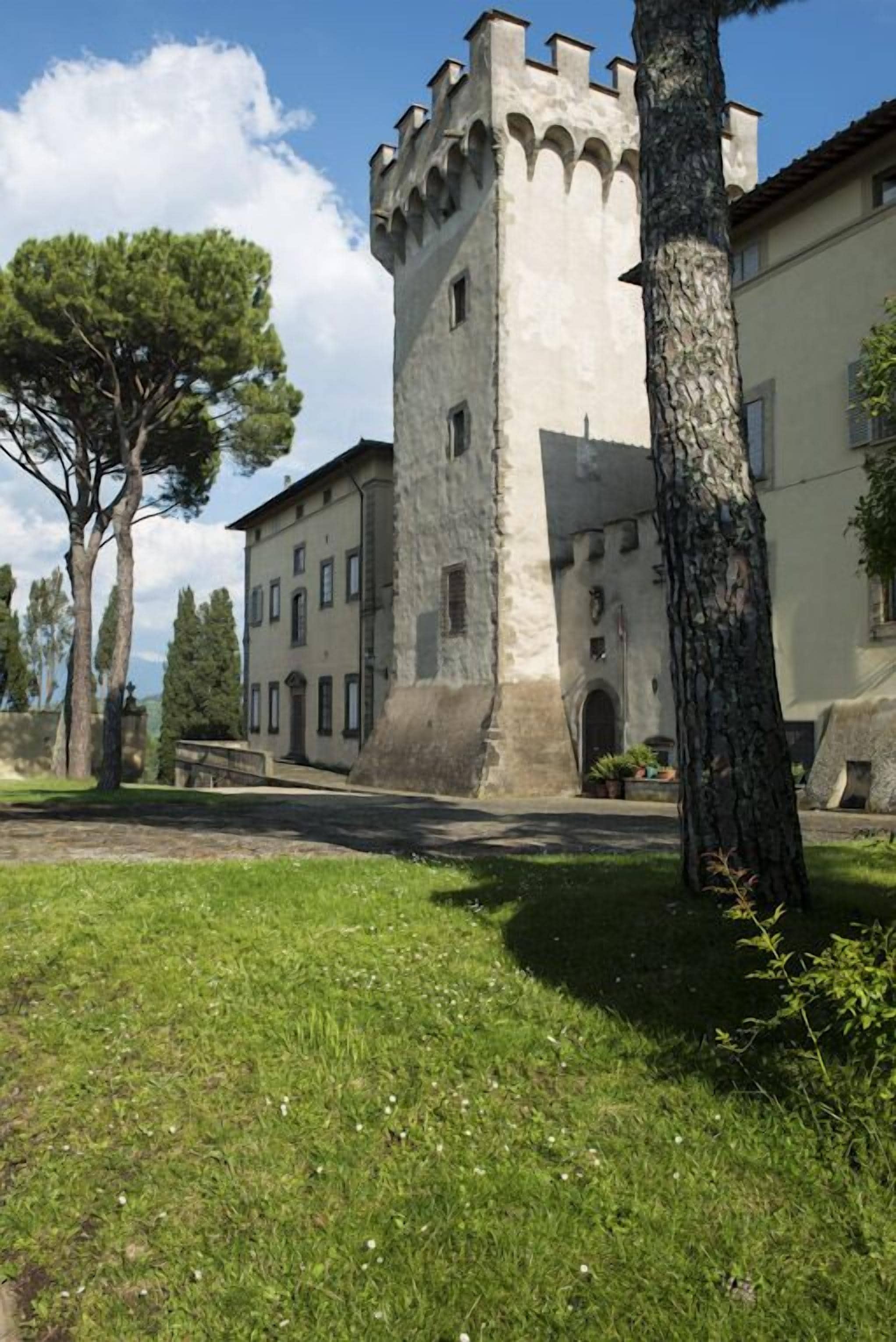 Um edifício histórico com uma torre, rodeado por árvores e um jardim bem cuidado.