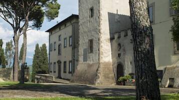 Um edifício histórico com uma torre, rodeado por árvores e um jardim bem cuidado.
