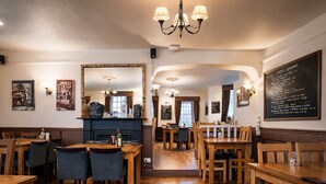 Interior de restaurante com mesas e cadeiras de madeira, área de bar e cardápio em lousa na parede.
