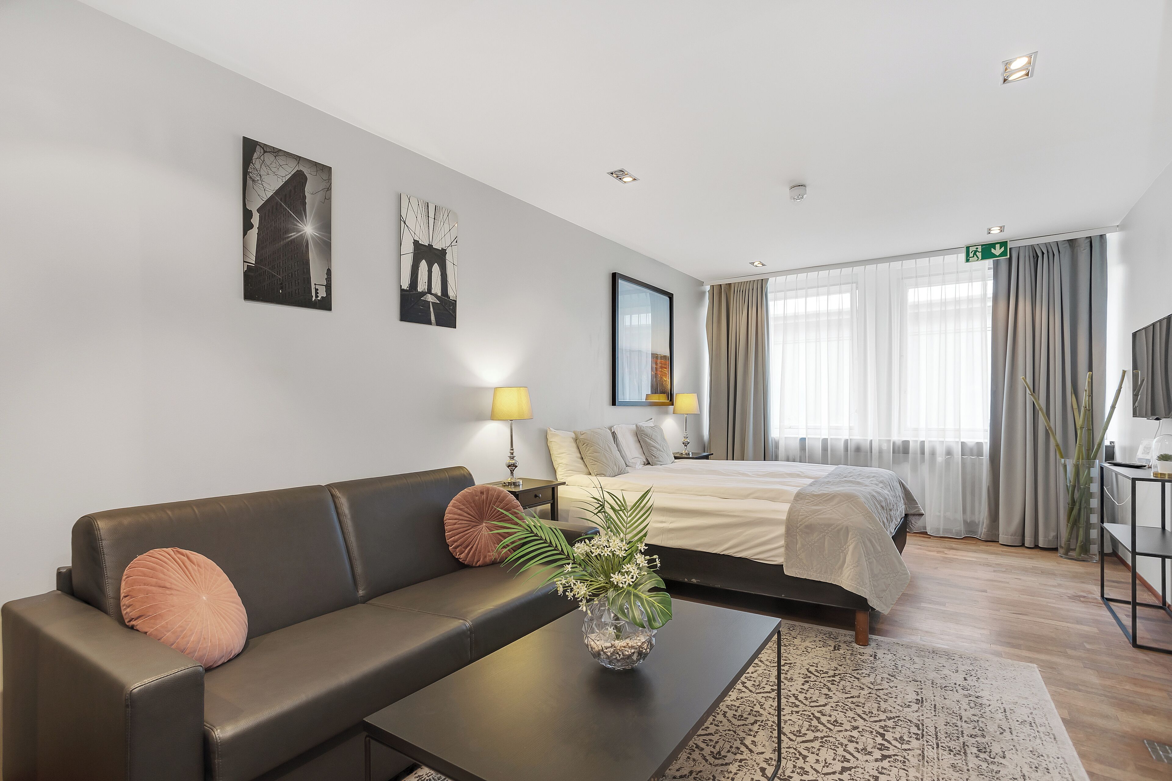 Quarto de hotel moderno com cama, sofá, mesa de centro com planta e obras de arte nas paredes.